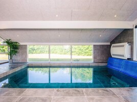 Piscina interior com paredes de vidro transparente, um banco acolchoado azul e um vaso de planta.