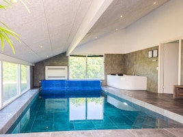 Piscina interna com um banco azul, área de spa branca e amplas janelas que proporcionam luz natural.