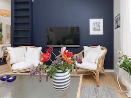 Uma sala de estar com dois sofás de vime, um vaso listrado com flores, uma televisão de tela plana e uma escada.