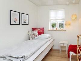 Quarto com cama, janela, uma mesinha e luzes na parede.
