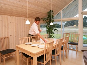 Uma área de refeições de madeira com uma mesa posta para quatro pessoas, rodeada por cadeiras com assentos acolchoados.