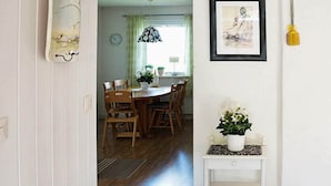 Um corredor leva a uma sala de jantar com cadeiras e mesa de madeira, um aparador branco com uma planta em vaso e uma obra de arte emoldurada na parede.