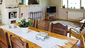 Uma sala de estar aconchegante com uma mesa de jantar de madeira, cadeiras, lareira, televisão e janela com cortinas.