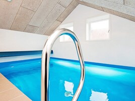 Piscina interior com escada de metal, água azul cristalina e chão em azulejo.