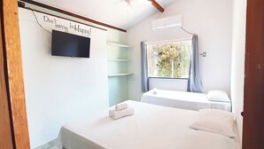 Quarto com cama, televisão na parede, janela com cortinas e prateleira fixada na parede.