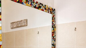Casa de banho com painel de azulejos decorativos, uma pia branca, espelho e uma planta.