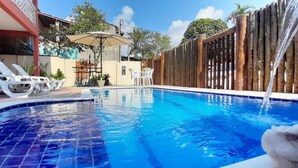 Piscina com cerca de madeira, espreguiçadeiras e mesa com guarda-sóis.