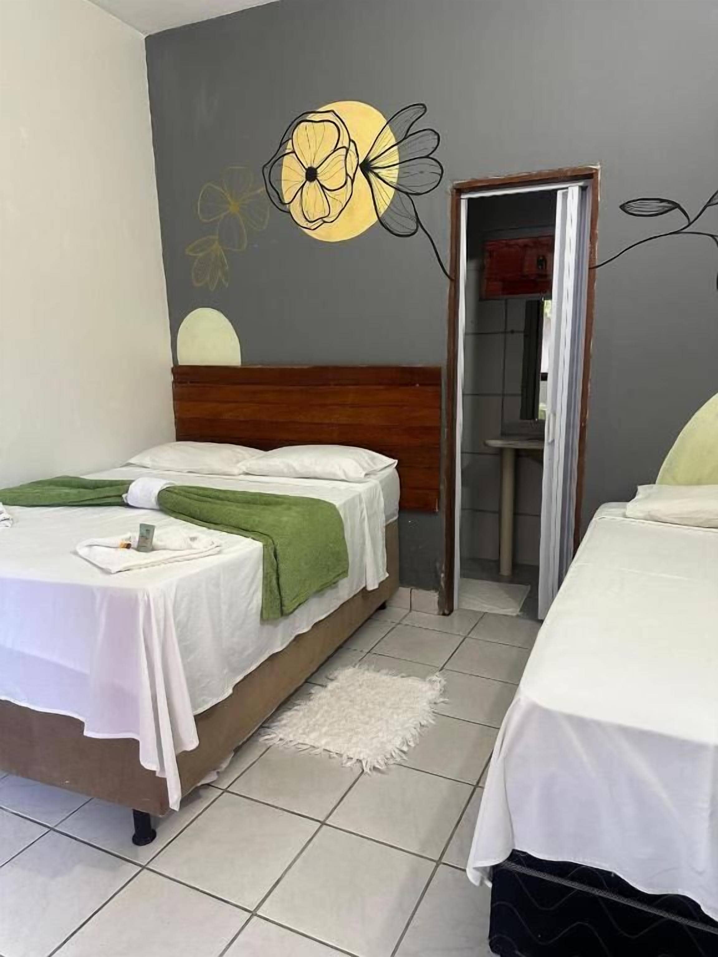 Quarto de hotel com duas camas, uma cabeceira de madeira, um tapete branco e uma parede com um mural floral.