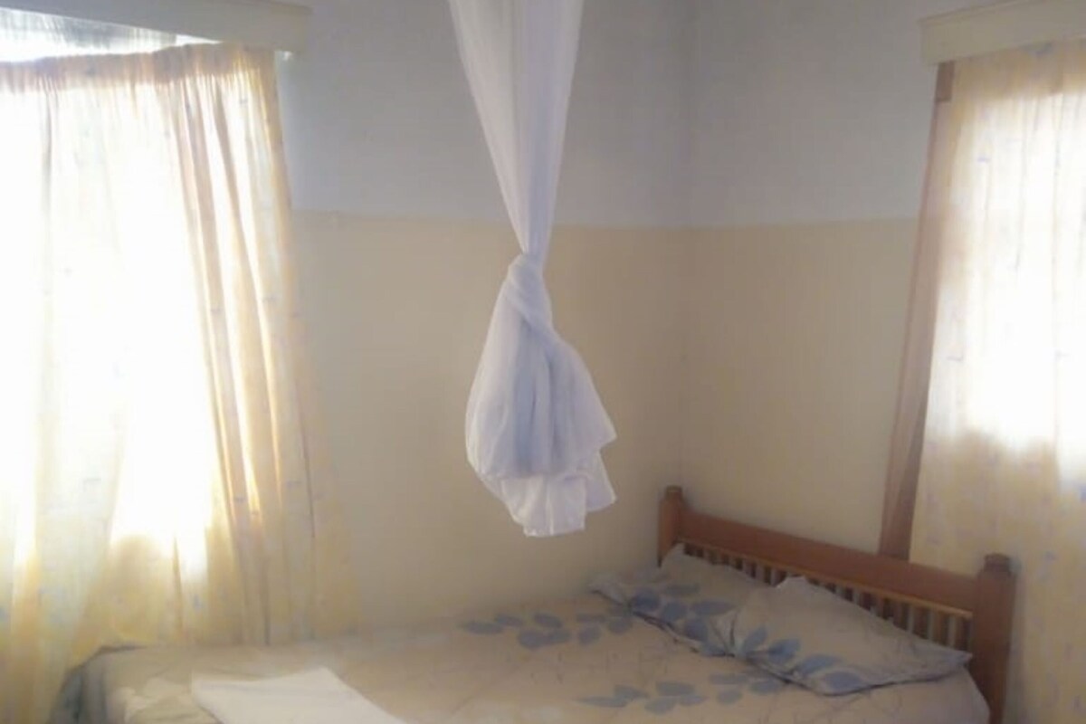Uma cama de solteiro com dossel, cabeceira de madeira e colcha estampada com flores.
