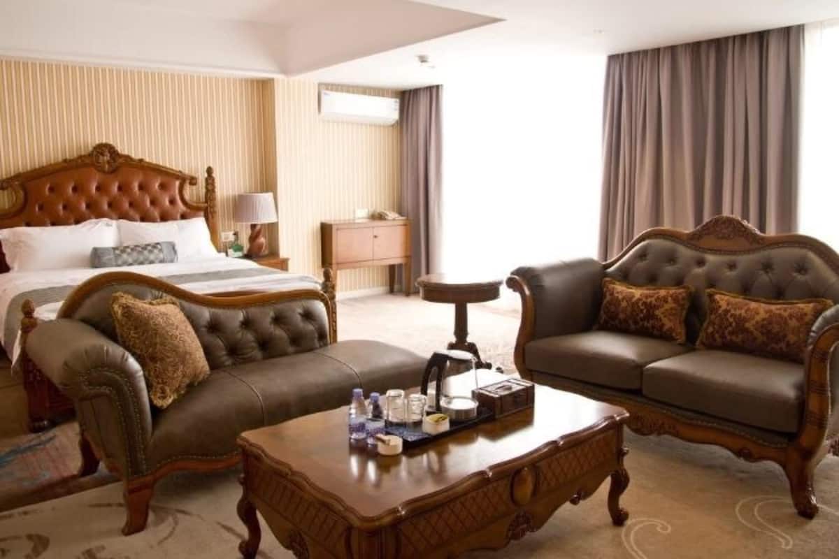 Quarto de hotel com uma cama grande, dois sofás, uma mesa de centro de madeira e uma mesa de cabeceira com abajur.