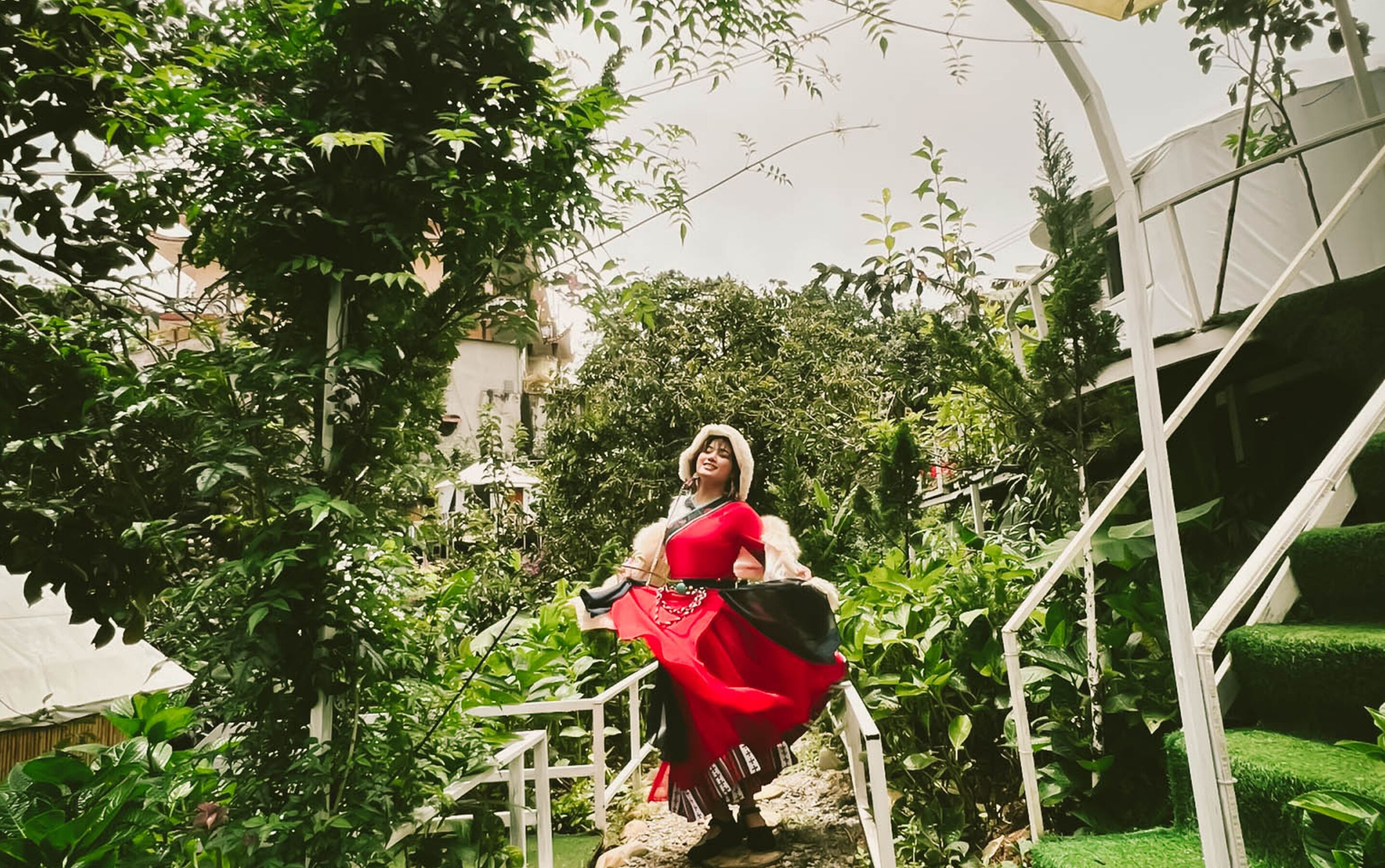 Uma pessoa vestida de vermelho caminhando sobre uma escadaria branca, rodeada por vegetação exuberante.