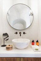 Um banheiro com um espelho redondo, uma pia branca e duas garrafas de shampoo.