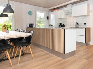 Cozinha moderna com ilha central, painéis de madeira e área de jantar com mesa e cadeiras.