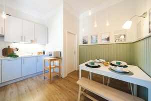 Cozinha moderna com armários brancos, uma mesa de madeira com um banco e um micro-ondas na bancada.