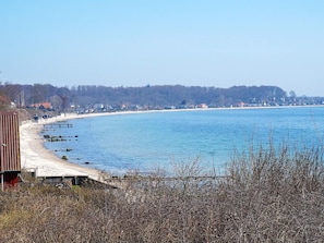 Vista costeira com uma praia de areia, um cais que se estende para a água e uma fileira de edifícios à beira-mar.