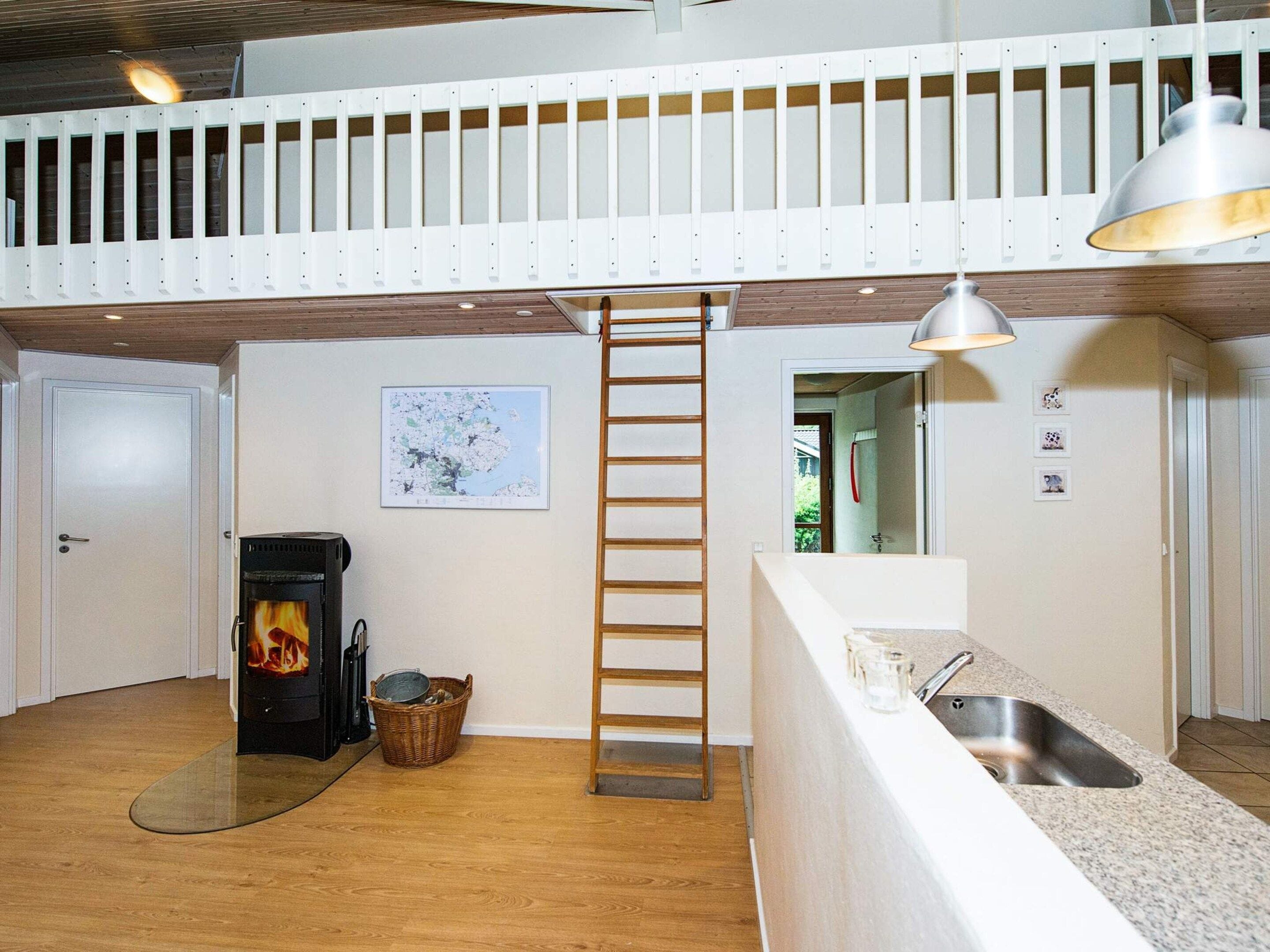 Um interior moderno com lareira, escada de madeira, cozinha e um mezanino.