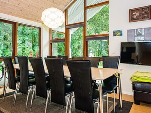 Uma sala de jantar com teto de madeira, janelas amplas e uma televisão.