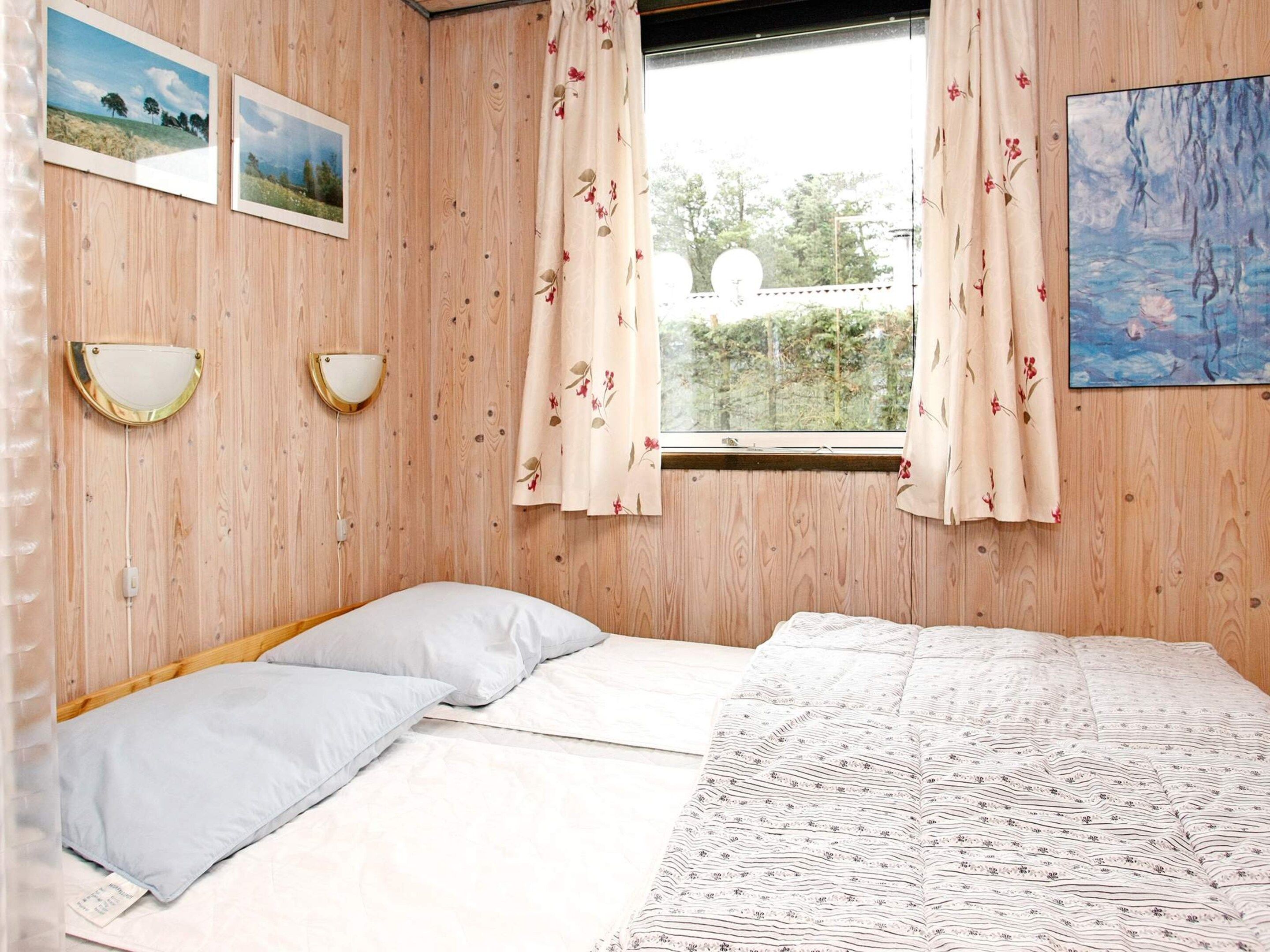 Quarto com cama, duas luminárias na parede, janela com cortinas e duas imagens emolduradas.