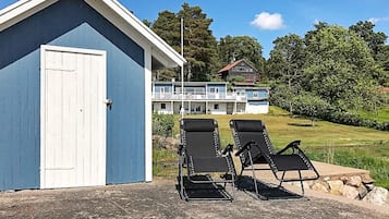 Um edifício com fachada azul, duas cadeiras de descanso pretas e vista para uma casa com varanda.