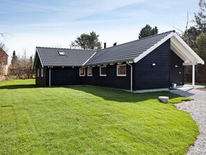 Uma casa moderna de dois andares, com telhado inclinado, gramado bem cuidado e entrada por um caminho de cascalho.