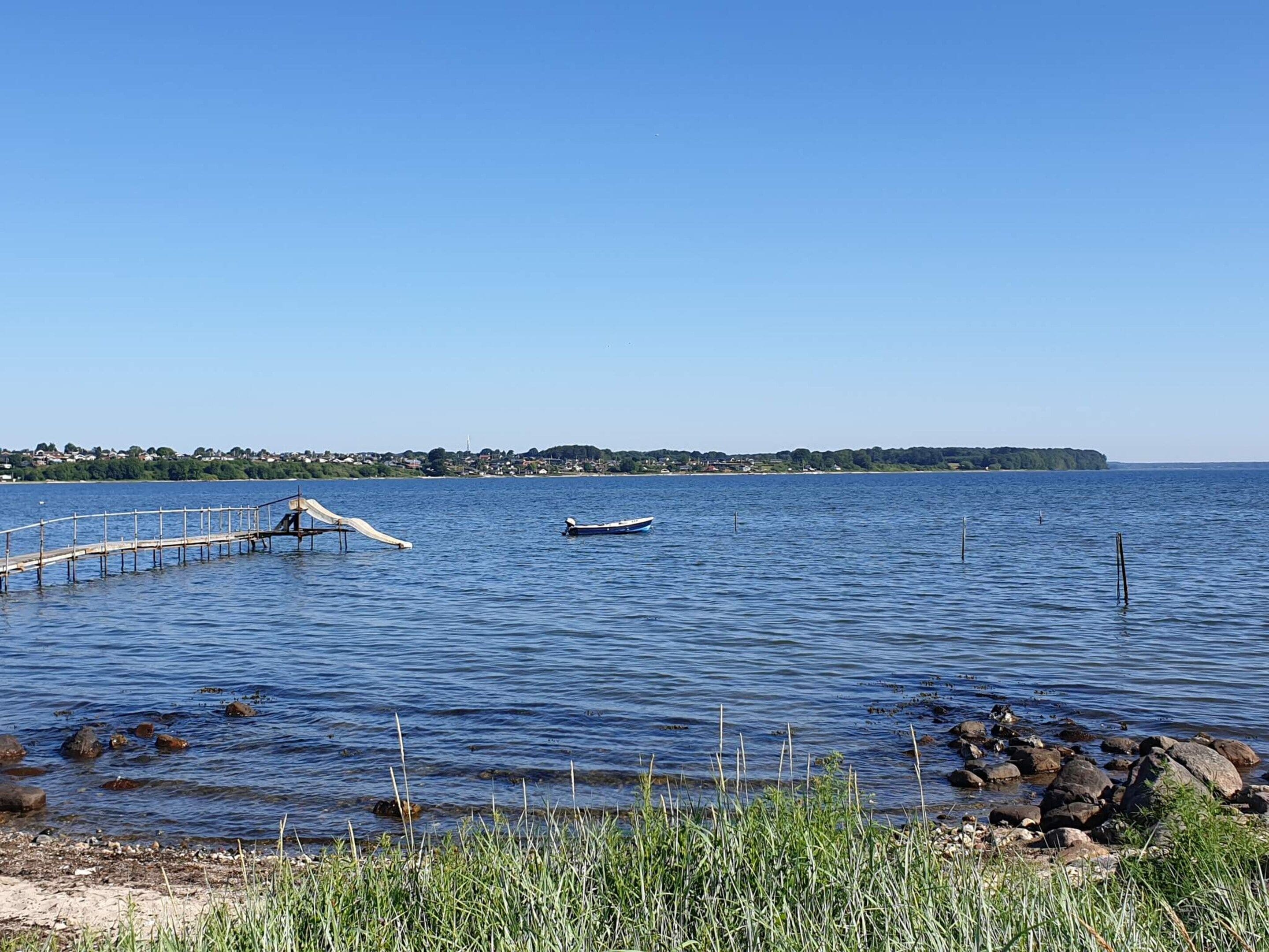 Um lago tranquilo com um cais que se estende pela água, cercado por pedras e vegetação.