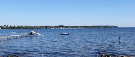 Um lago tranquilo com um cais que se estende pela água, cercado por pedras e vegetação.