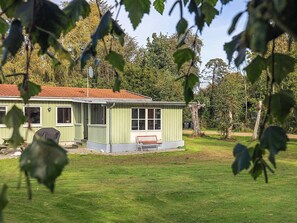 Um pequeno edifício térreo com fachada verde e telhado vermelho, cercado por gramado e árvores.