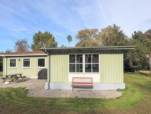 Um pequeno edifício térreo com fachada verde, um banco em frente e uma mesa de piquenique por perto.