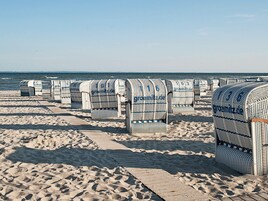 Bungalôs de praia com números, dispostos em fileiras numa praia arenosa, com o mar ao fundo.