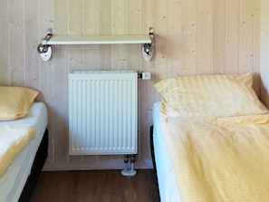 Quarto com duas camas, um radiador e parede de madeira.