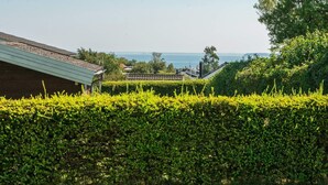 Seio bem cuidado em frente a um edifício com telhado inclinado, vista clara do mar e uma linha distante de árvores.