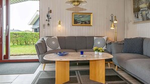 Uma sala de estar moderna com um sofá cinza, uma mesa de centro redonda de madeira e um tapete estampado.