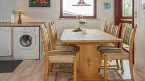 Uma área de refeições com mesa e cadeiras de madeira, uma máquina de lavar, uma janela com vista e um quadro na parede.