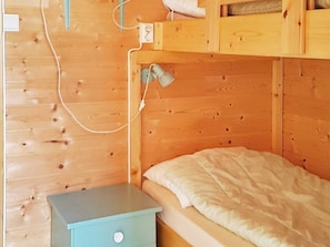 Uma cama beliche com cabeceira de madeira, uma mesinha de cabeceira e um cobertor branco.