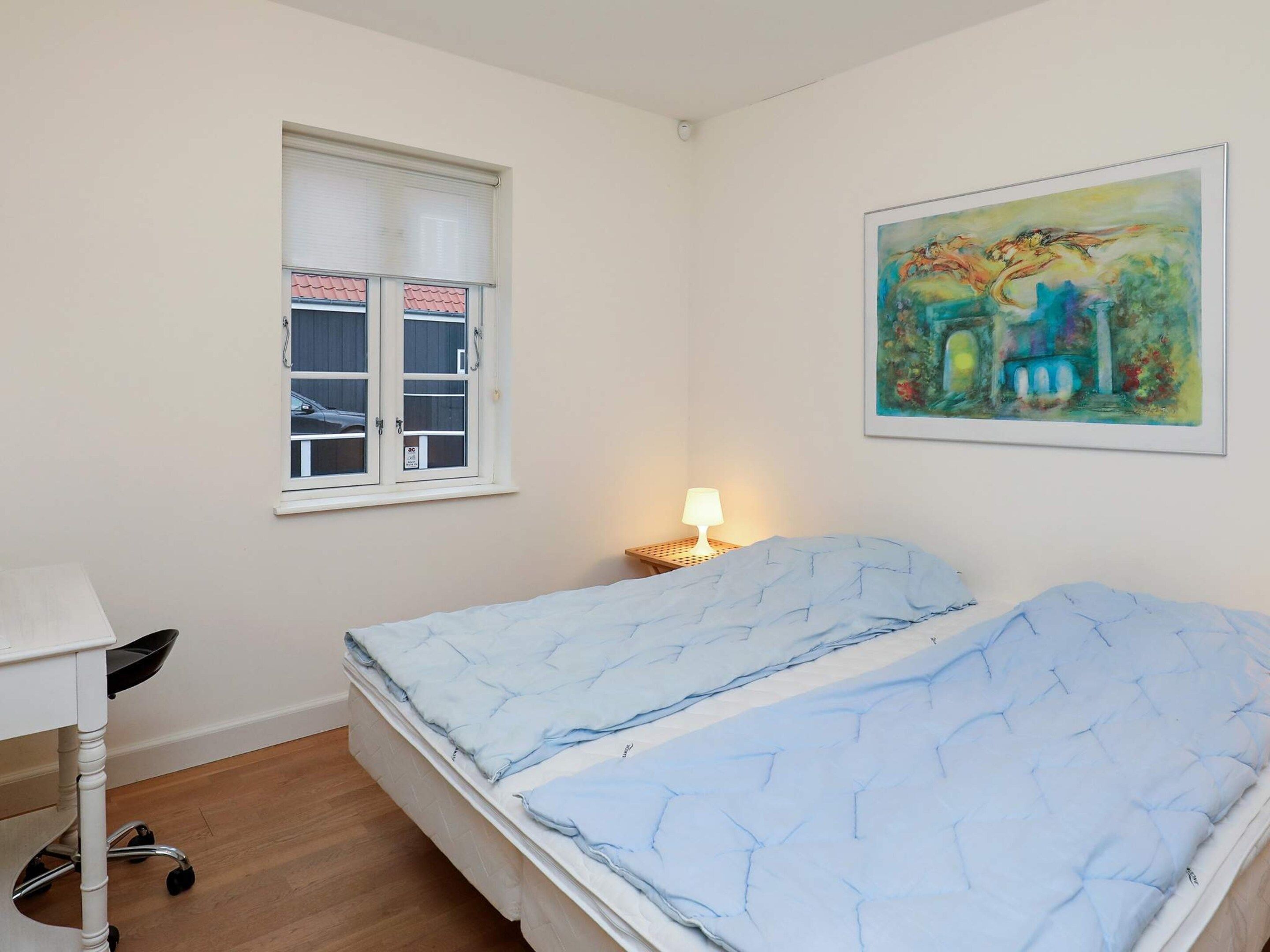 Quarto com cama, escrivaninha, janela e um quadro.