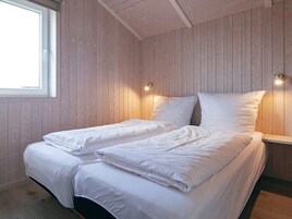 Uma cama de solteiro com roupa de cama branca num quarto com paredes de madeira e uma janela.