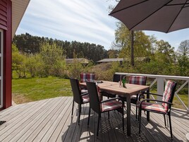 Um terraço ao ar livre com mesa e cadeiras, cercado por vegetação e árvores.