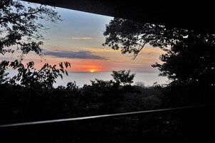 Vista do pôr do sol pela janela, com árvores emoldurando a paisagem.