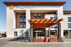 Um hotel moderno com um destaque para a placa 'La Quinta', apresentando uma entrada coberta e área de estar externa com jardineiras.