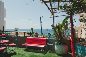 Terraço com um banco vermelho, plantas em vasos e vista para o mar.