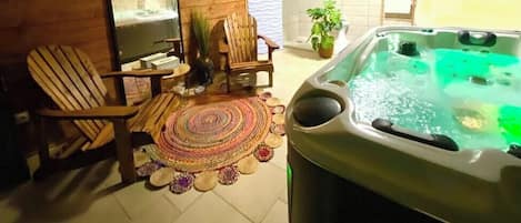 Uma cadeira de madeira, um tapete redondo trançado e uma banheira de hidromassagem com borbulhas.