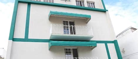 Um hotel com fachada verde e branca, uma varanda com corrimão branco e uma placa indicando que é um hotel.