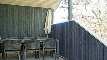 Uma área externa para refeições com mesa, cadeiras, um painel de madeira e vista para árvores.