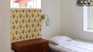 Quarto com uma cama de solteiro, cômoda, luminária na parede e janela com vista para um prédio vermelho.