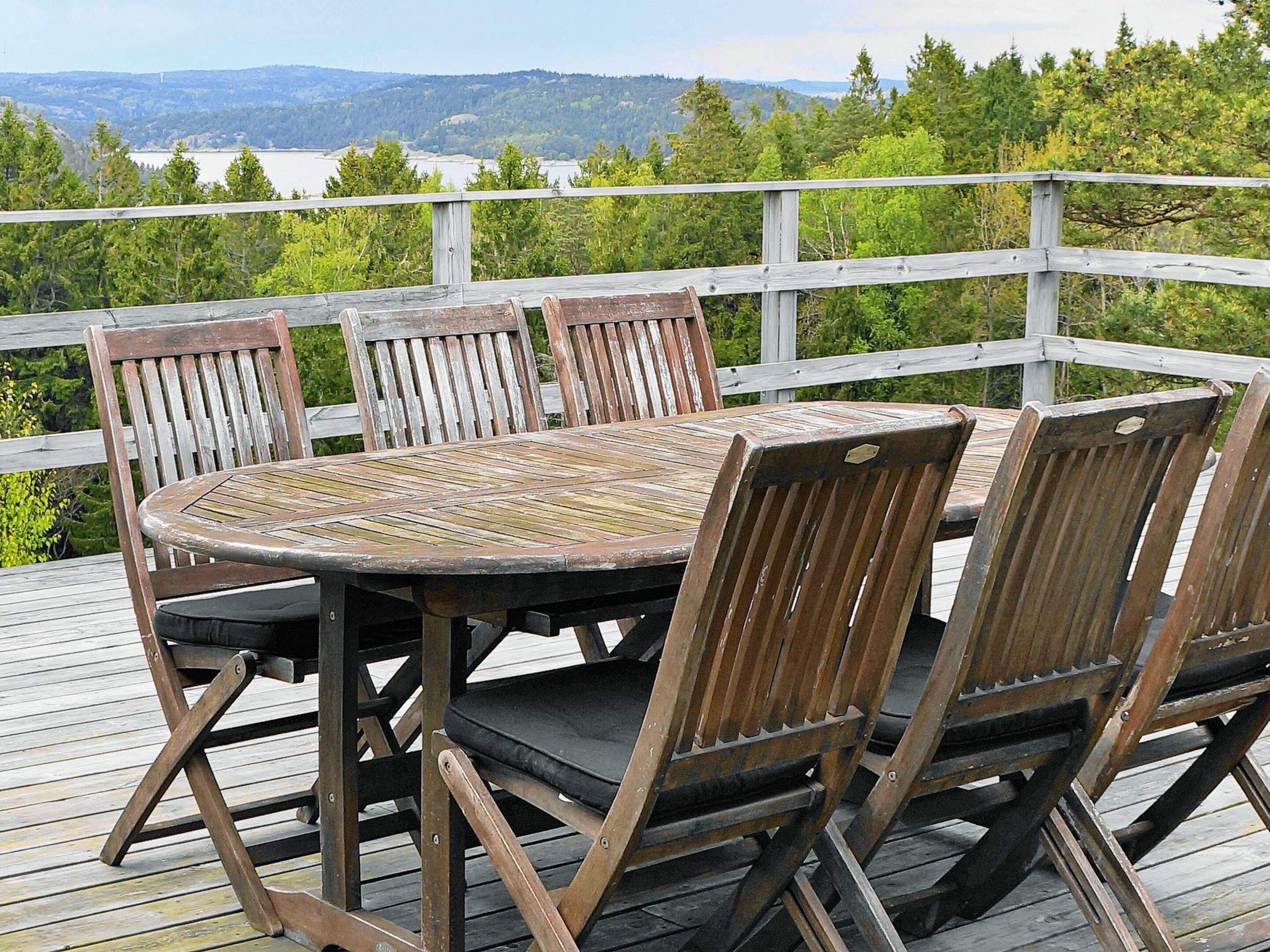 Um deck de madeira com uma mesa redonda e cadeiras, com vista para um lago e colinas arborizadas.
