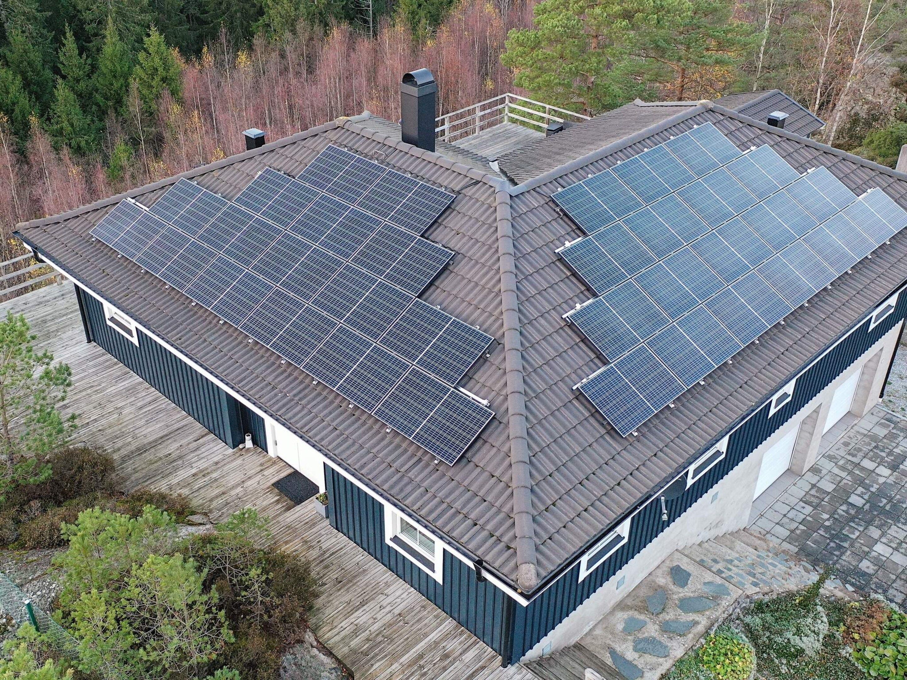 Um edifício com telhado inclinado coberto por painéis solares, rodeado por árvores.