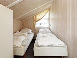 Uma cabana pequena, com um único quarto, duas camas, paredes de madeira e uma janela com cortinas.