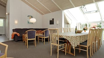 Uma sala de jantar com uma mesa posta para 8 pessoas, rodeada por cadeiras de madeira, um sofá e um lustre.