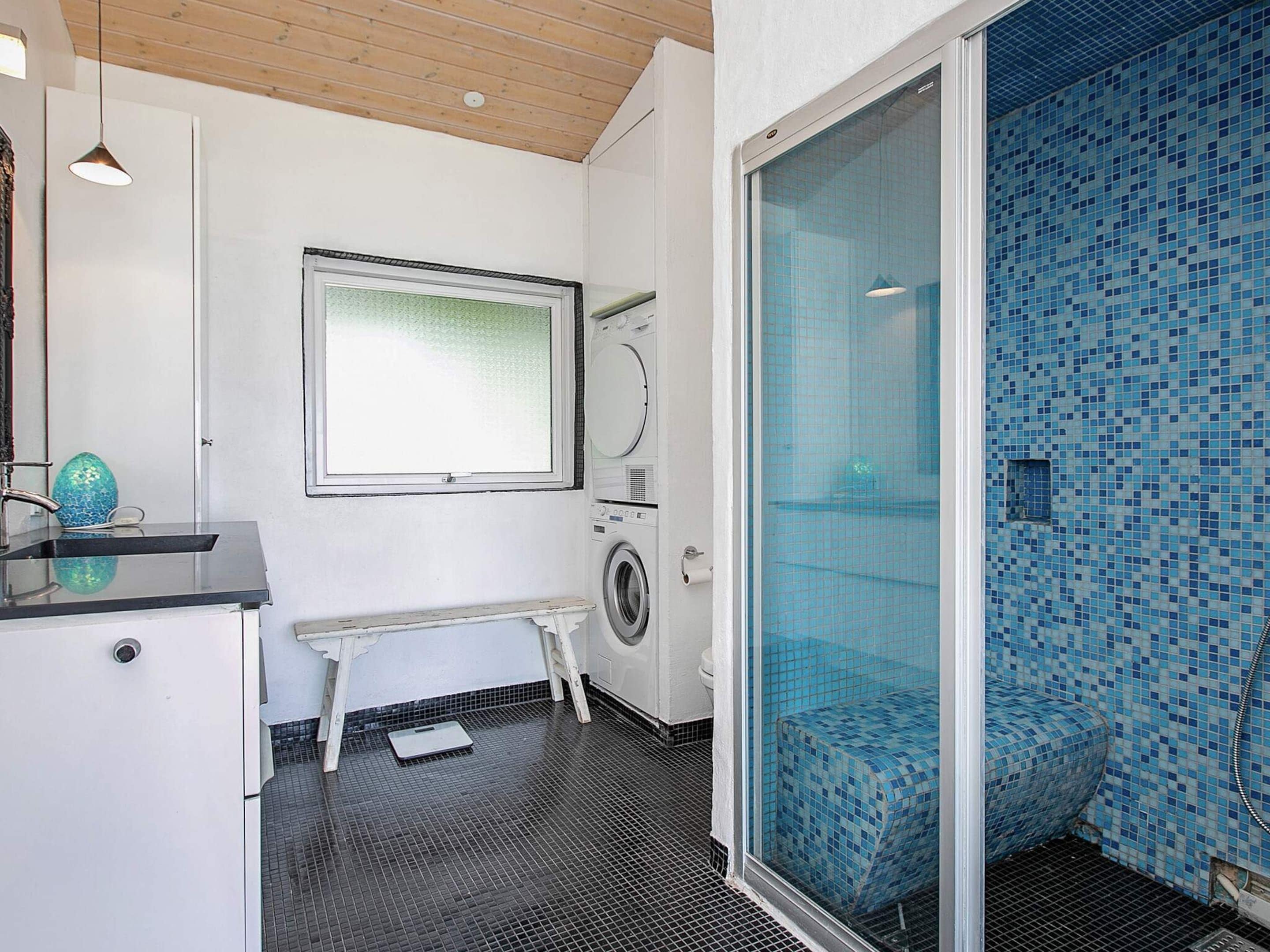 Um banheiro compacto com máquina de lavar, um banco e chuveiro revestido com azulejos azuis.