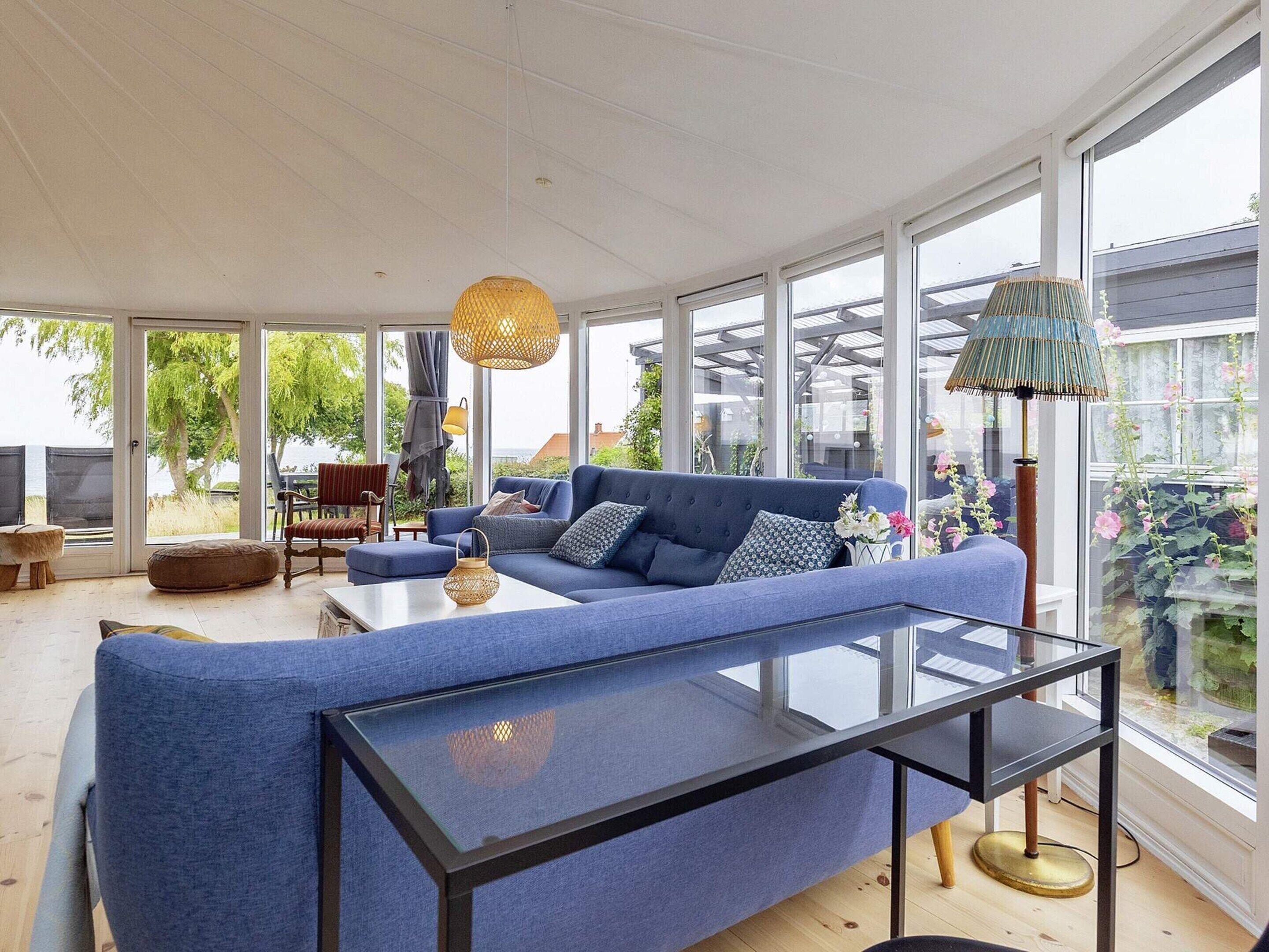 Uma sala de estar moderna com um sofá azul, uma mesa de centro de vidro e grandes janelas com vista para o exterior.